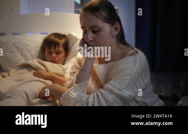Young sad woman worried about her little sick son sleeping in bed ...
