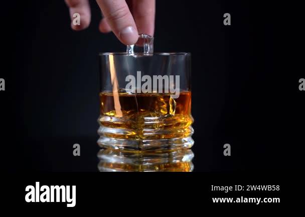 Glass of whiskey with ice cube. Alcohol pouring in the glass from the ... Glass of whiskey with ice cube. Alcohol pouring in the glass from the ...