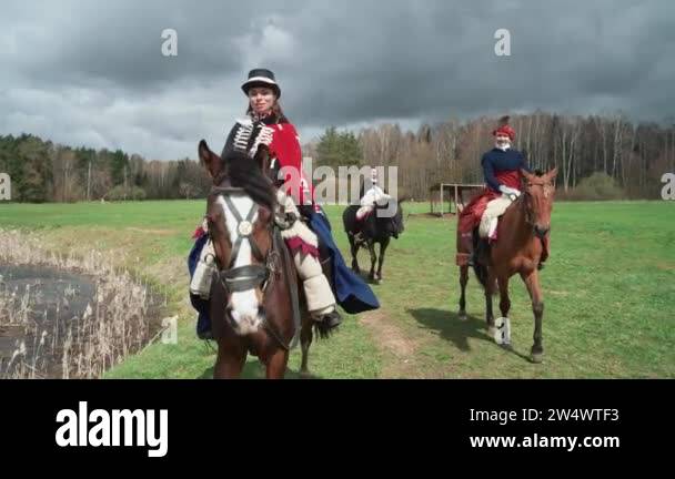 Females in a bright medieval costumes rides a horses through a field ...