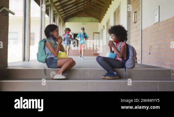 Multi ethnic group of school children wearing face masks, sitting on ...