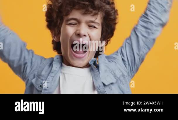 Excited young boy enjoying win, raising hands and shouting, orange ...