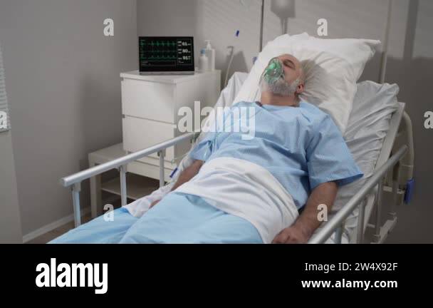 Senior male patient lying in a hospital bed wearing oxygen mask. The ...