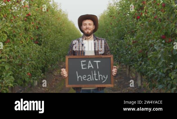 Eat healthy concept. Young positive man gardener showing board with ...