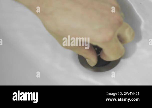 The hand pulls the rubber stopper from the sink, the water drains into ...