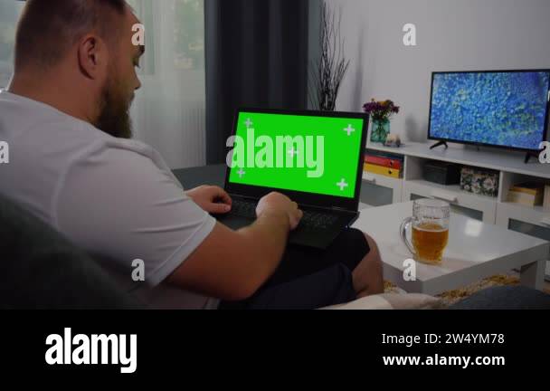 Man sitting on sofa Using Laptop with Greenscreen and Chroma Key. Mock ...