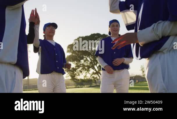 Diverse group of female baseball players on sunny pitch, taking a break ...