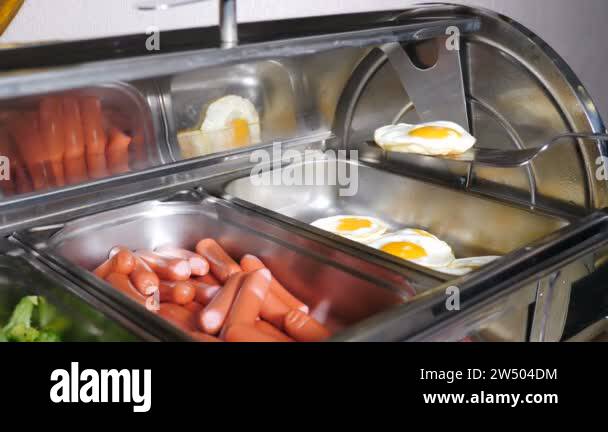 Buffet heated trays with sausages, boiled broccoli and fried eggs in ...