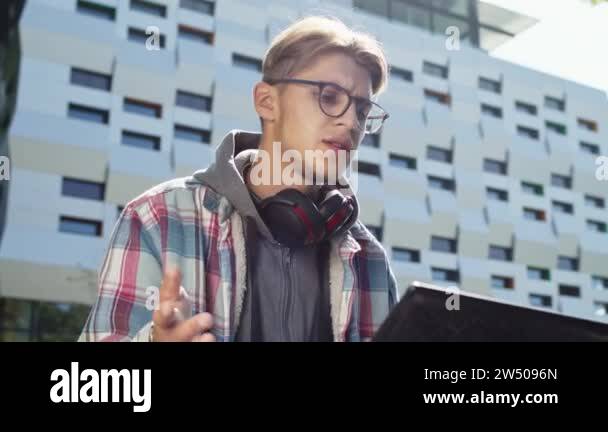 Young Guy With Glasses Sitting On The Street With Laptop On His Lap And ...