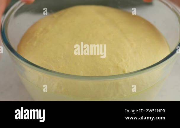 Female hands kneading raw yeast dough in a glass bowl, sunlight from ...