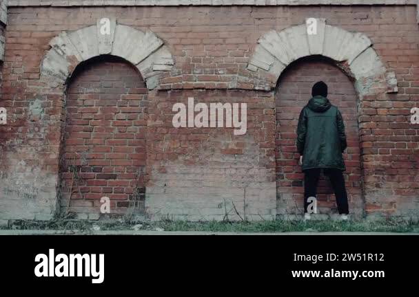 Rear view of a man in black clothes standing against red brick wall ...