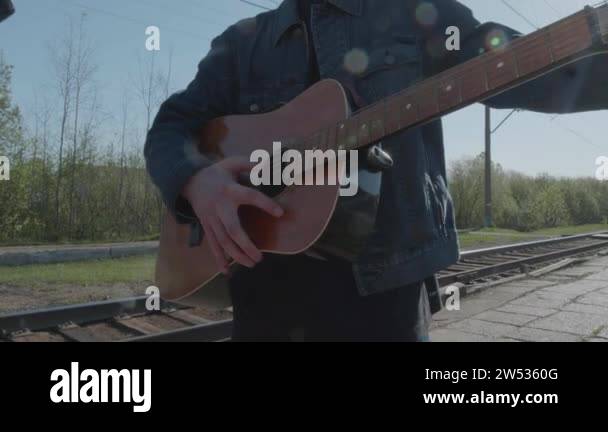 A man in a denim jacket tunes an acoustic guitar while standing next to ...
