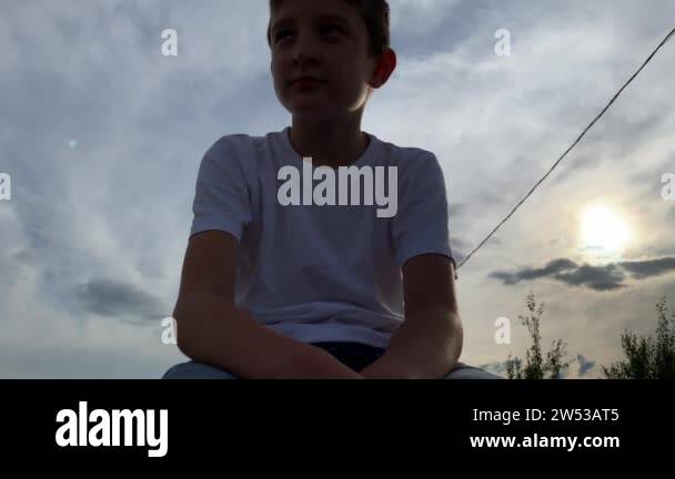 A lonely sad boy sitting outdoors on a bench at sunset, unhappy ...