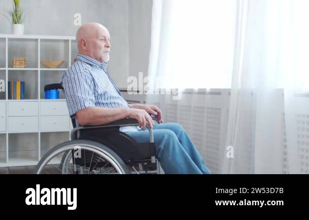 Disabled old man is sitting in a wheelchair at home alone. A ...