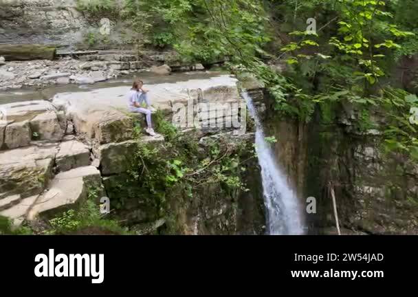 young woman sitting near Waterfall in Maniava. Carpathian Mountains ...