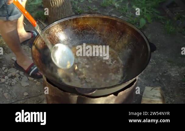 Cooking food over a fire in a cauldron. Outdoor cooking. Stirring hot ...
