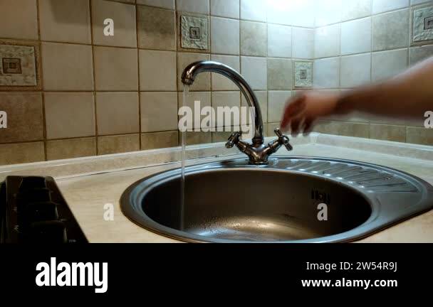 Man opens water tap, and then closes it back. Tap water flows from tap ...