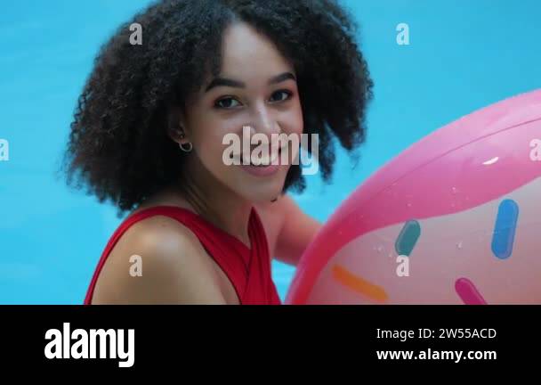Portrait of beautiful American curly girl in red swimwear in pool ...