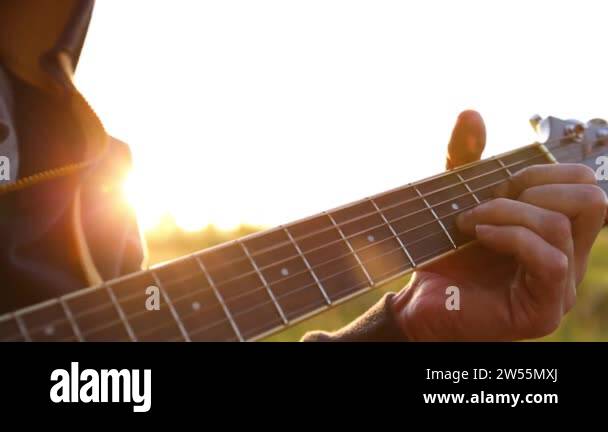 Man plays a guitar and sings outdoor songs at sunset. Hand on the ...