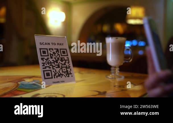 Woman scans the QR code displayed by the merchant with their phone to ...