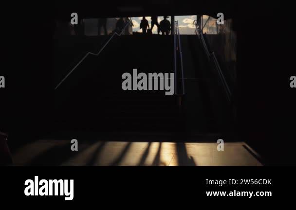 People walk through dark underpass near stairs at susnet, underground ...