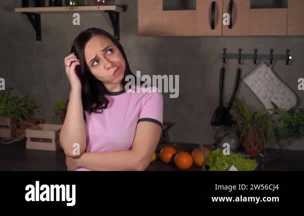 Confused young woman scratching her head a kitchen. Portrait female ...