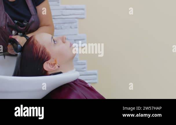 Young woman sits, putting head over sink during hair care procedure in ...