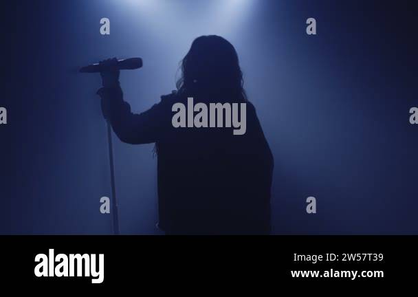 Backlit silhouette of singer vocalist girl standing in dark nightclub ...