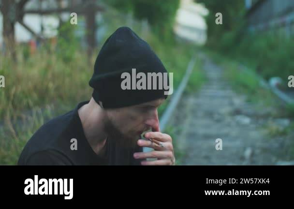 Homeless man smoking cigarette blows smoke, siting on the railway ...