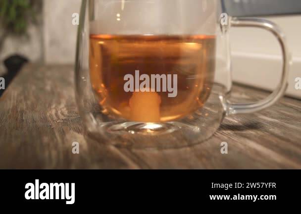 Close up view female hands add sugar cube in fresh-brewed tea, stir spoon sweetener in glass cup ...