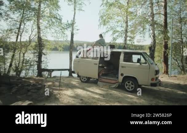 Zoom in wide shot of woman sitting on roof of camper van and enjoying ...