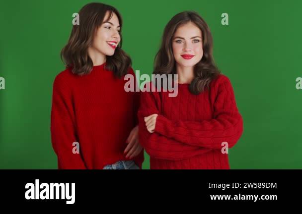 Two attractive girls wearing red sweaters are sharing secrets standing ...