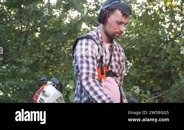 Young Caucasian farmer uses gasoline powered electric scythe to trim ...