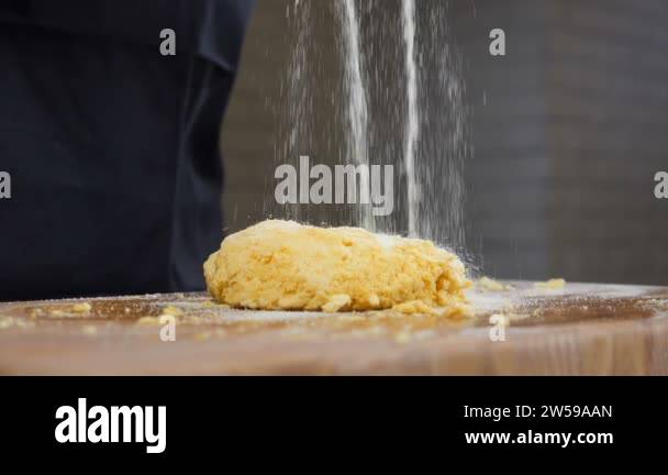 Sifting flour on dough on kitchen table while kneading. Chef is making ...