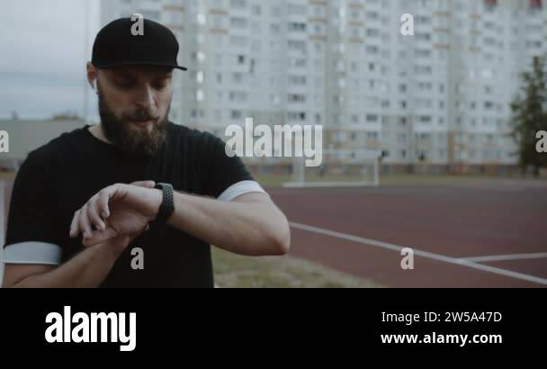 Young motivated male athlete preparing to run on track, setting timer ...