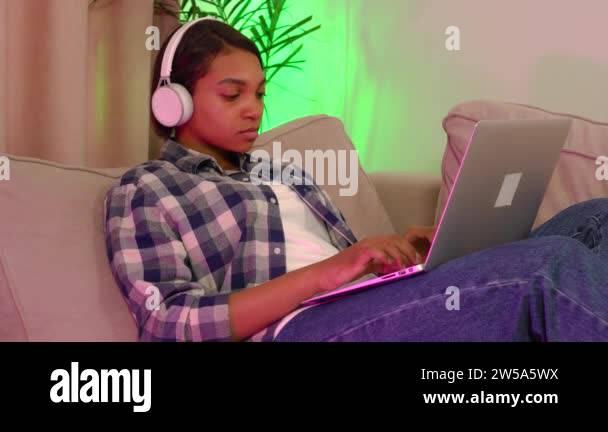 Tired woman lying on the couch with a laptop listening to music ...