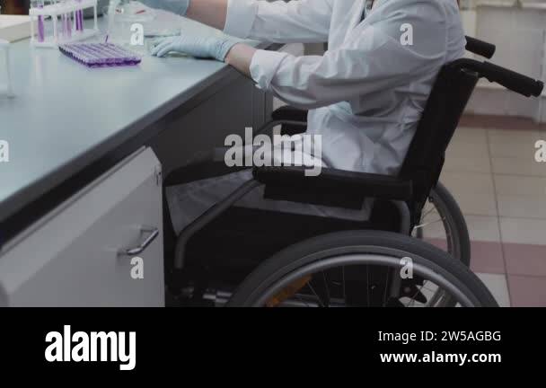 Tilt up slowmo of disabled female scientist in wheelchair using dropper ...