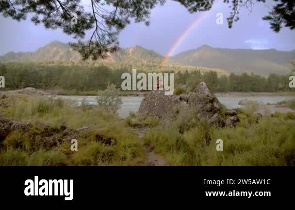 Altai shaman in national dress sits on rock next to river and plays ...