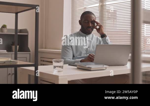 Locked-down of tired young African man sitting at desk in office ...