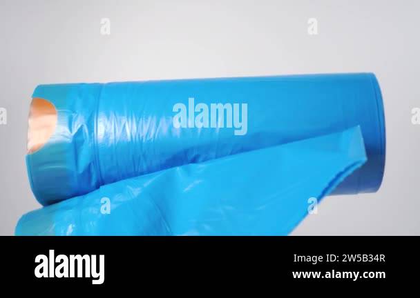 Hand holds new roll of blue garbage bags close up from recycled ...
