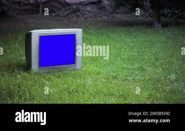 Old Television with Blue Screen in the Grass. Zoom In. You can replace ...