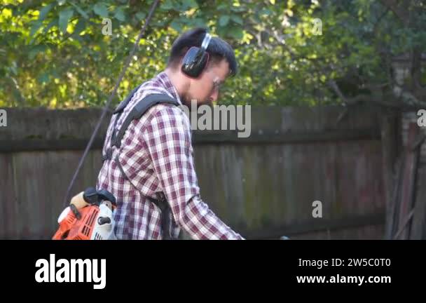 Young Caucasian farmer uses gasoline powered electric scythe to trim ...