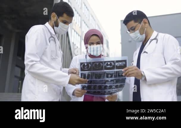 Three doctors neurologists, wearing uniform and mask, posing outdoors ...