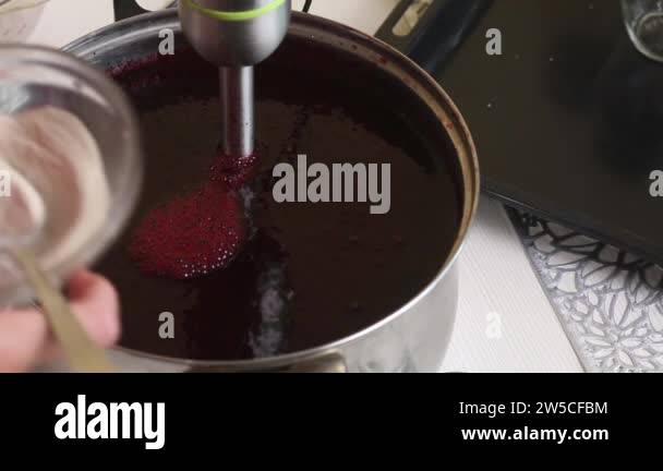 A woman adds agar agar to blueberry and sugar puree. Making blueberry ...
