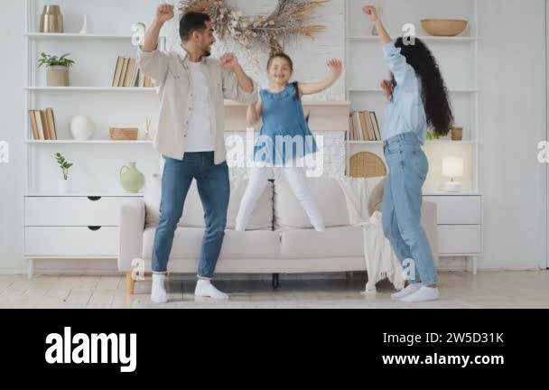 Spanish family dancing at home living room. Young parents move to music ...