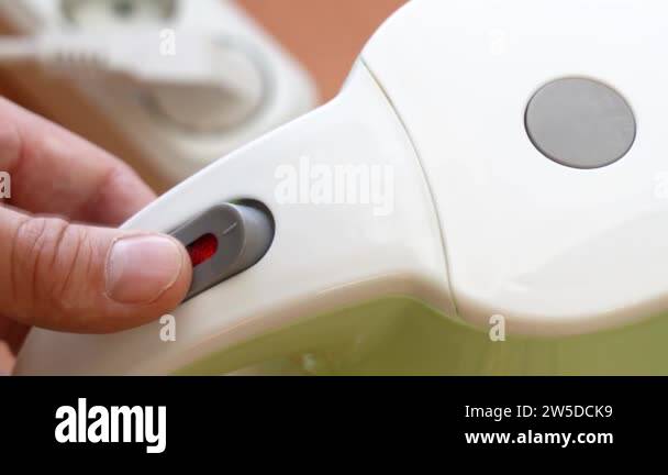 A mans hand presses a button in the kettle to disconnect and pulls out ...
