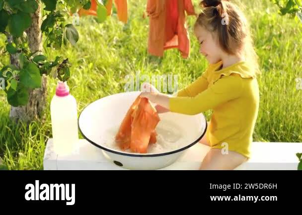 A girl washes clothes with liquid washing powder from a bottle in a ...