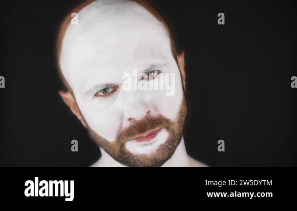 A mime man in a white mask depicts emotions. Man on a black background ...