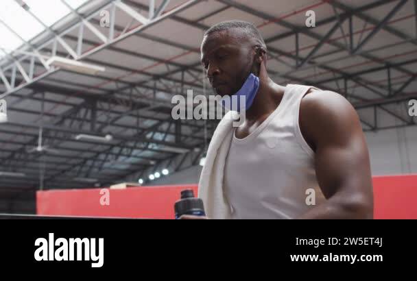 African american man wearing lowered face mask drinking at gym ...