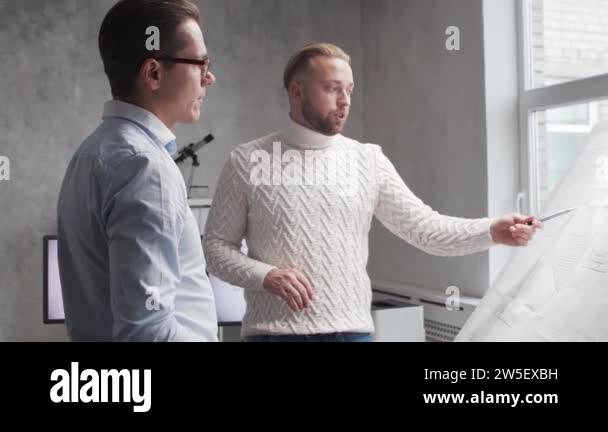 Architect and his colleague work in loft using drawing board. Workplace of young engineer in ...