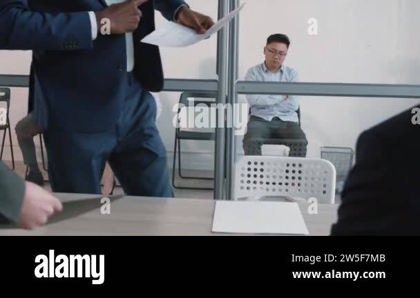 Job applicants sitting in hallway behind glass wall of conference room ...